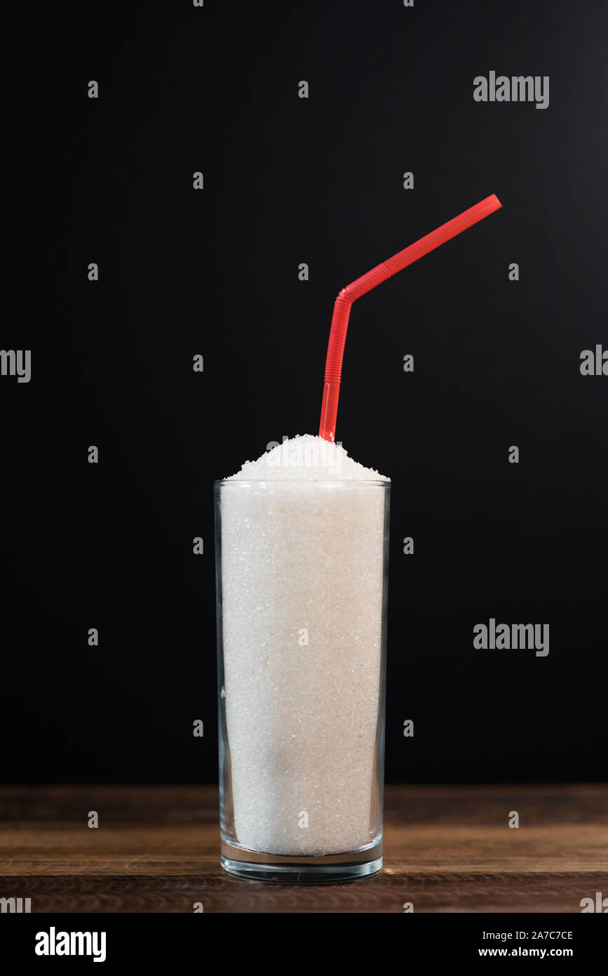 A glass full of white sugar with straw against black background ...