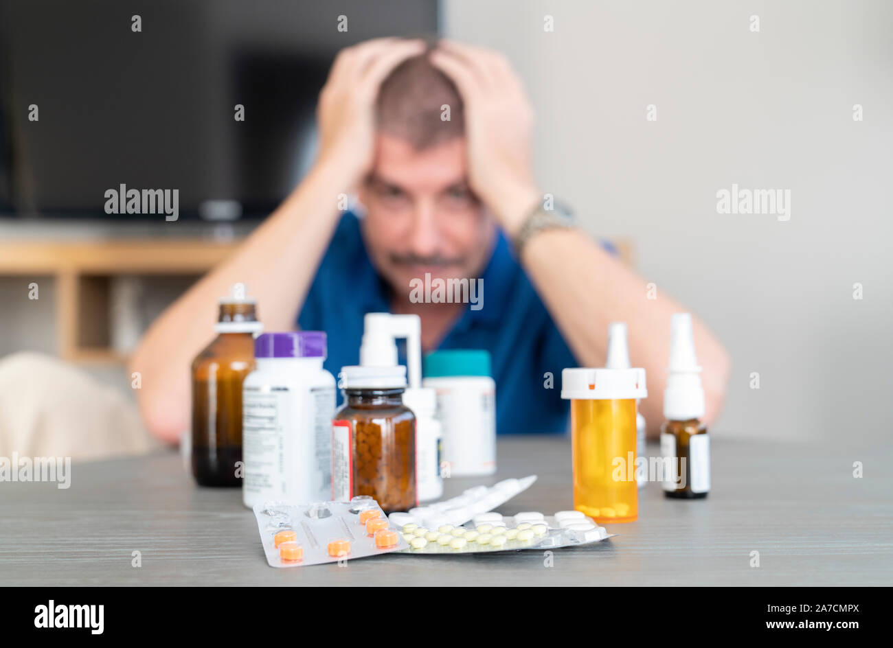 bottles of medication on the table with a man holding his head at the ...