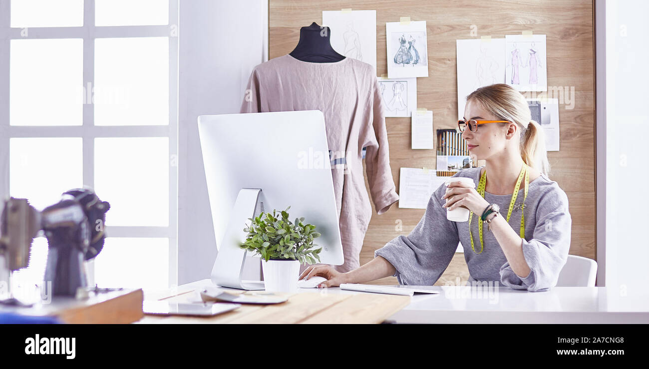 Attractive fashion designer working in office, leaning on desk, drawing ...