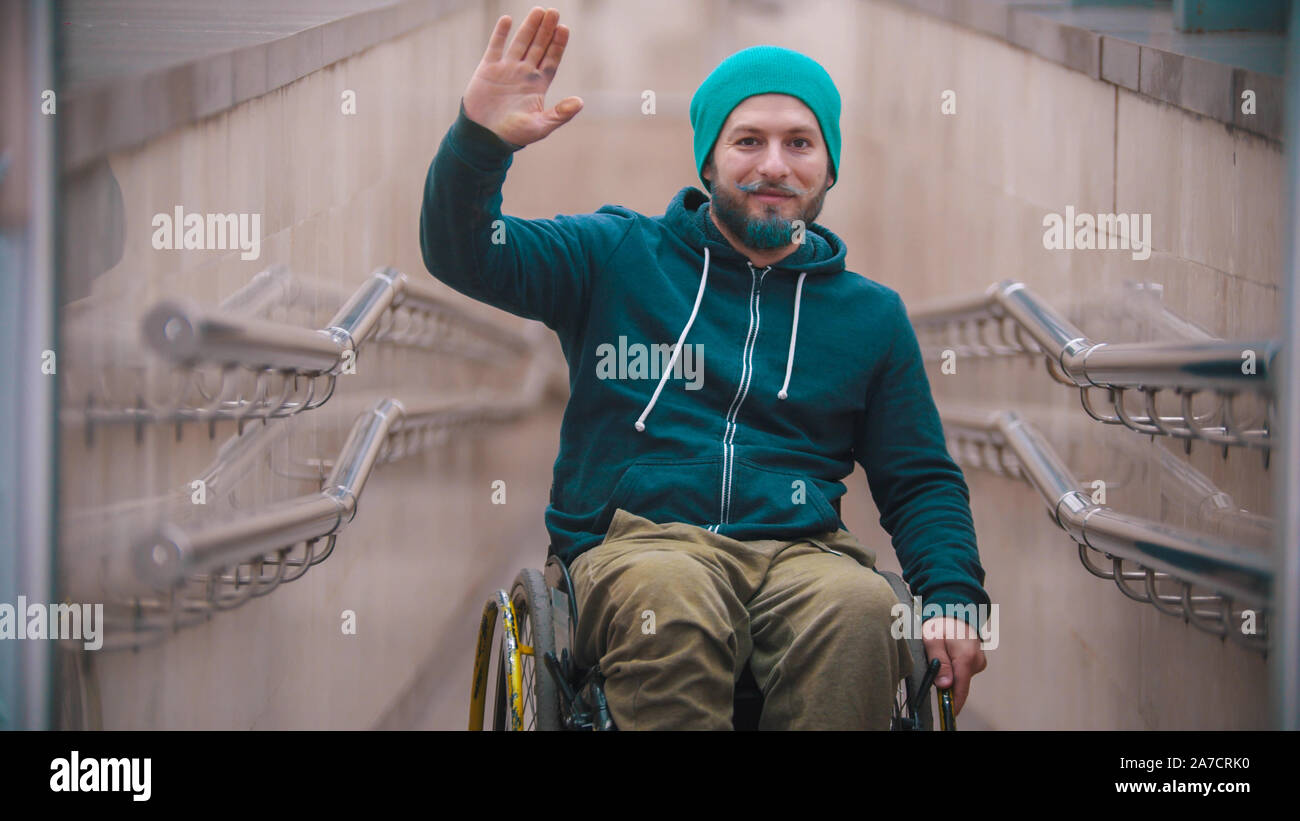 Disabled man in wheelchair waving with his hand. Mid shot Stock Photo ...
