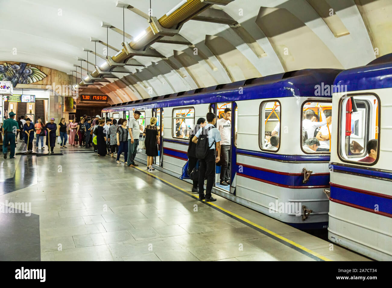 Commuters boarding a train while two female cleaners sweep the platform ...