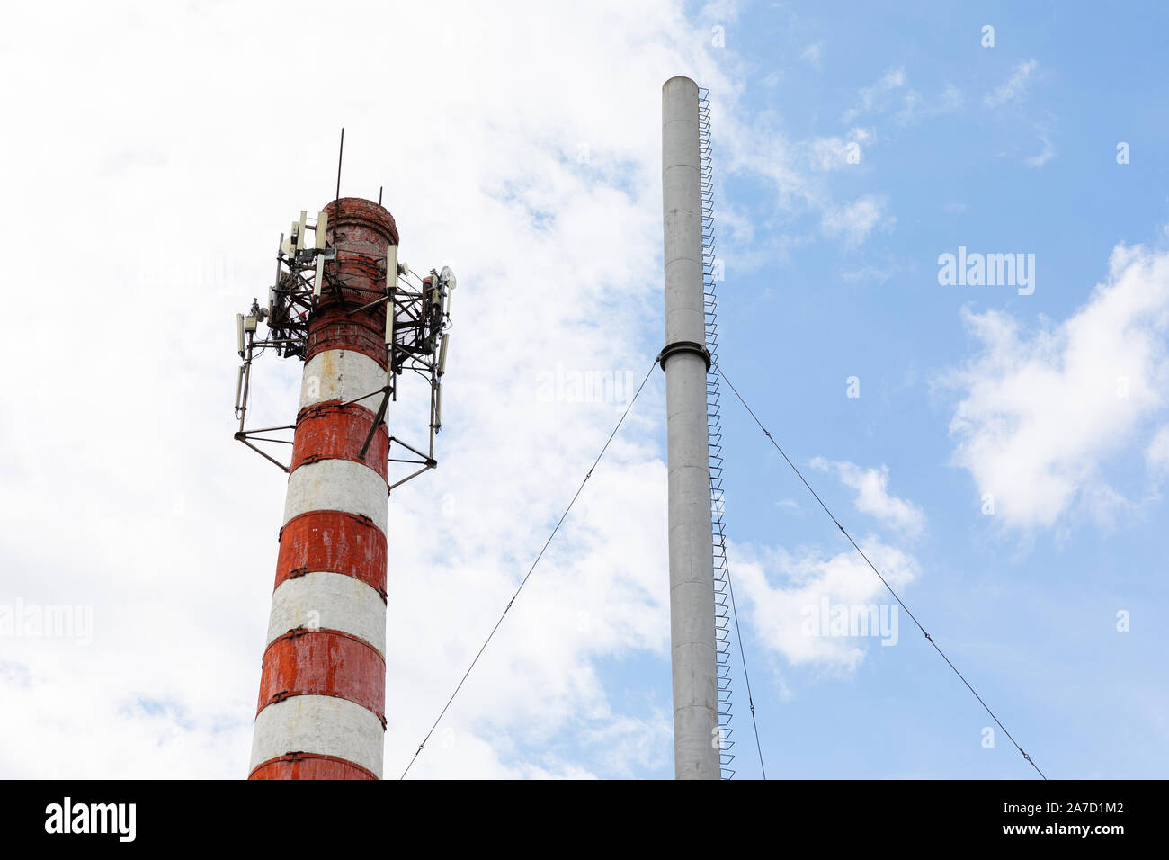 Red white chimney with steel installation nearby with tree in blue sky ...