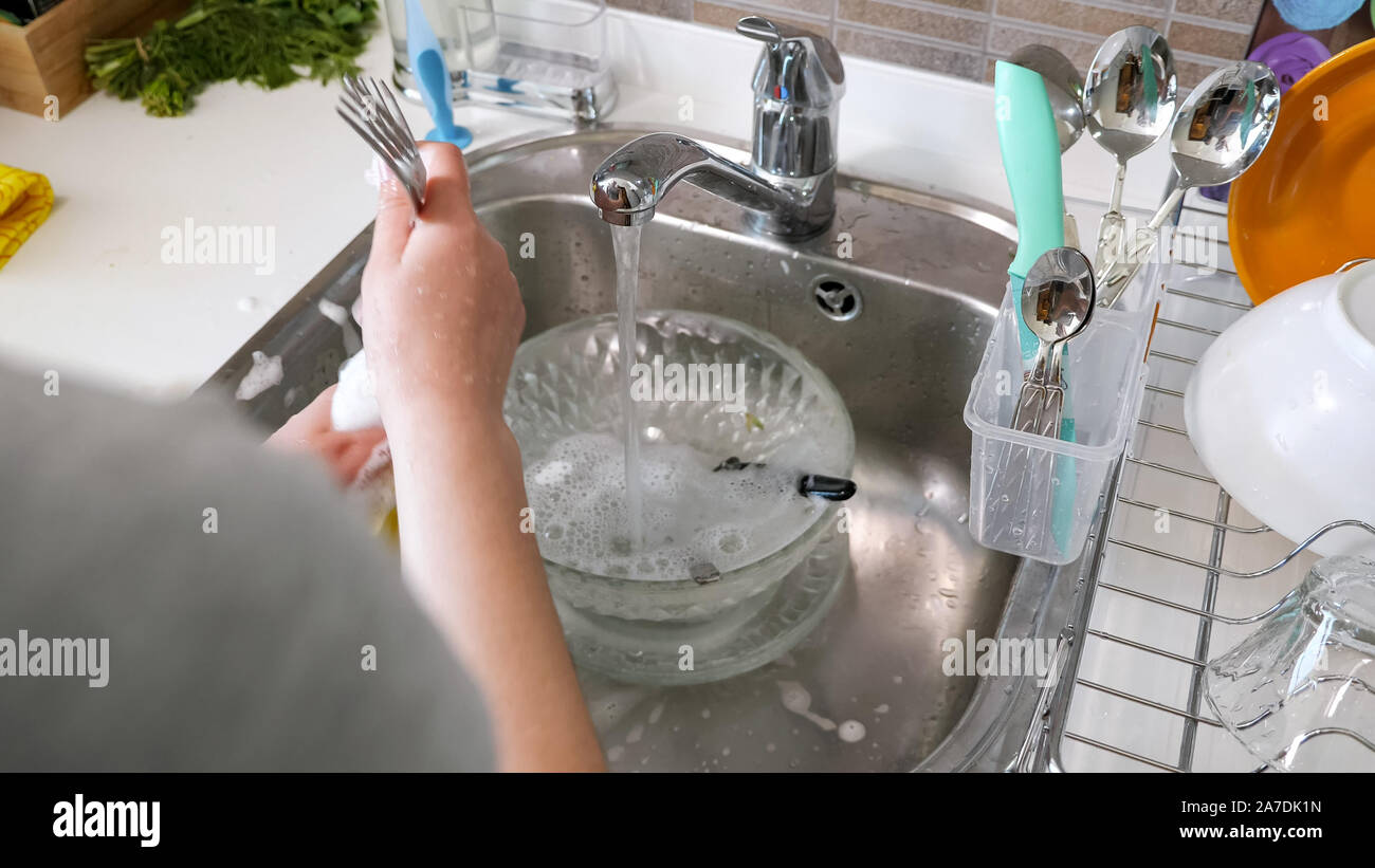 Woman is washing cutlery forks by hands soaping sponge with detergents ...