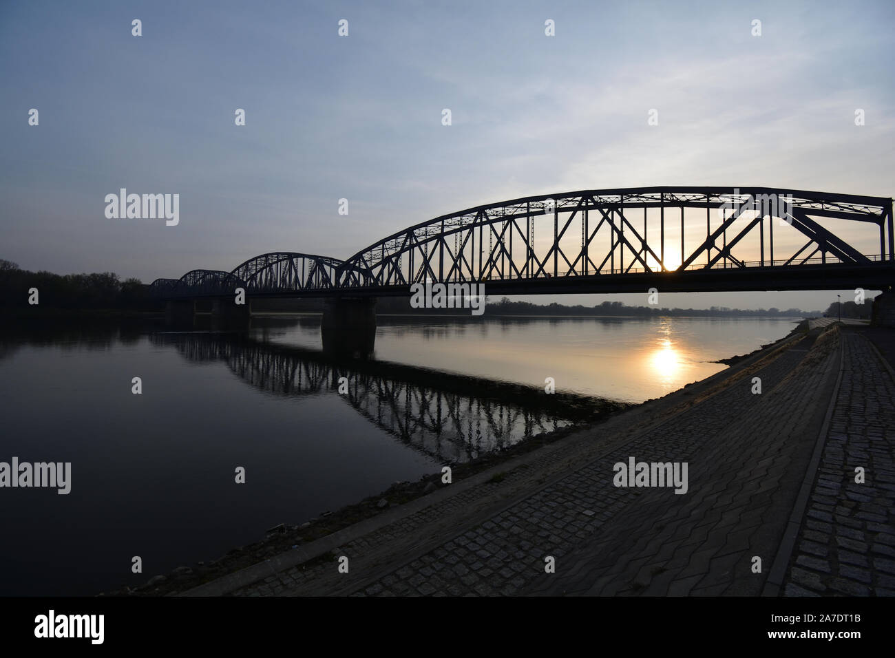 Truss bridge against sunset reflecting on the river below Stock Photo ...