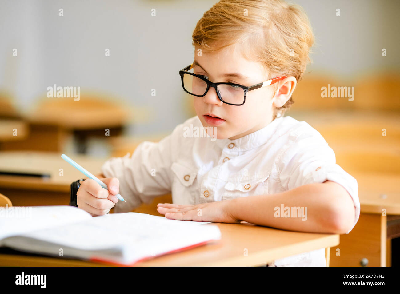 Seven years old child with glasses writing his homework at school. Boy ...