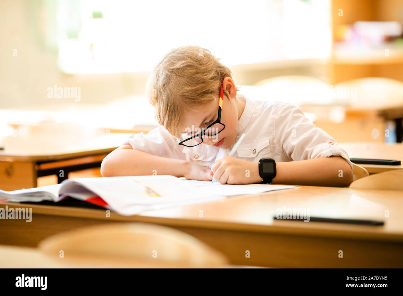 Seven years old child with glasses writing his homework at school. Boy ...