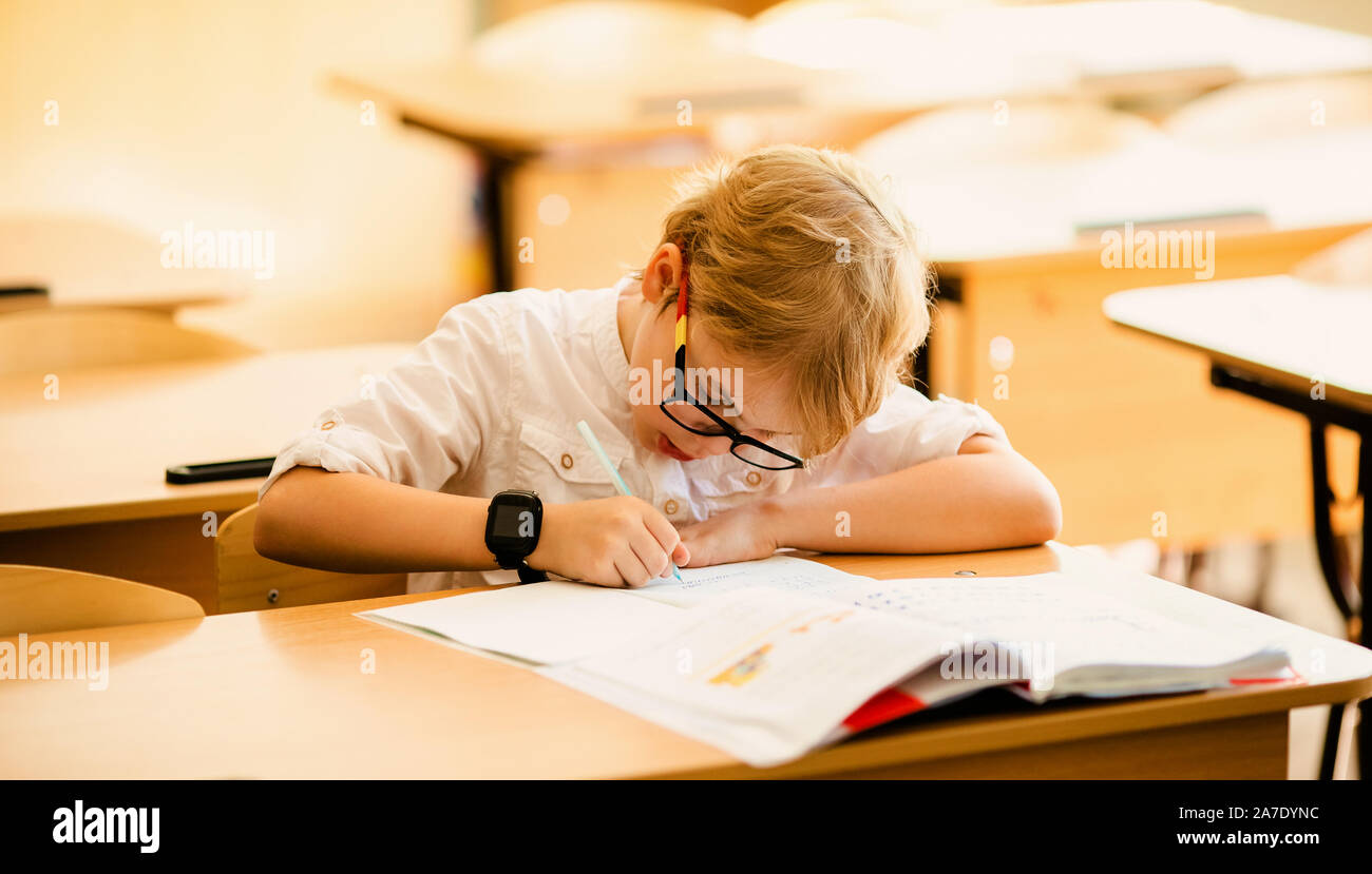 Seven years old child with glasses writing his homework at school. Boy ...