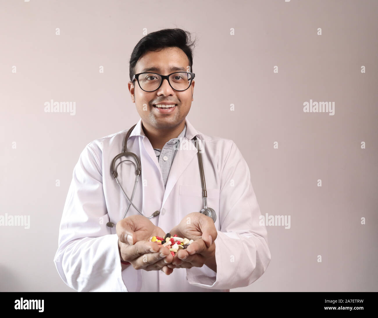 male indian doctor in white coat and stethoscope with medicine pills ...