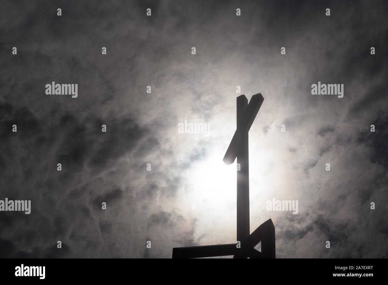 A Christian crucifix atop a church silhouetted by rays of light from ...
