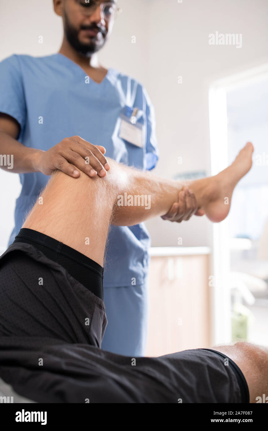 Contemporary medical specialist in uniform holding sick leg of his ...