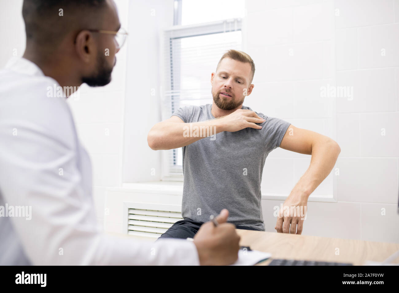 Young sick patient touching his shoulder while showing doctor where it ...