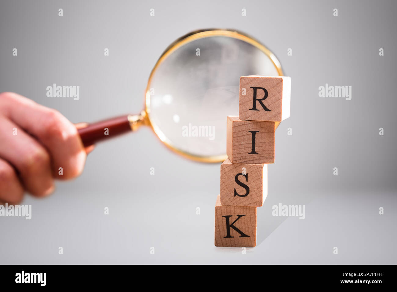 Businessperson's Hand Holding Magnifying Glass Over The Stacked Of Risk ...