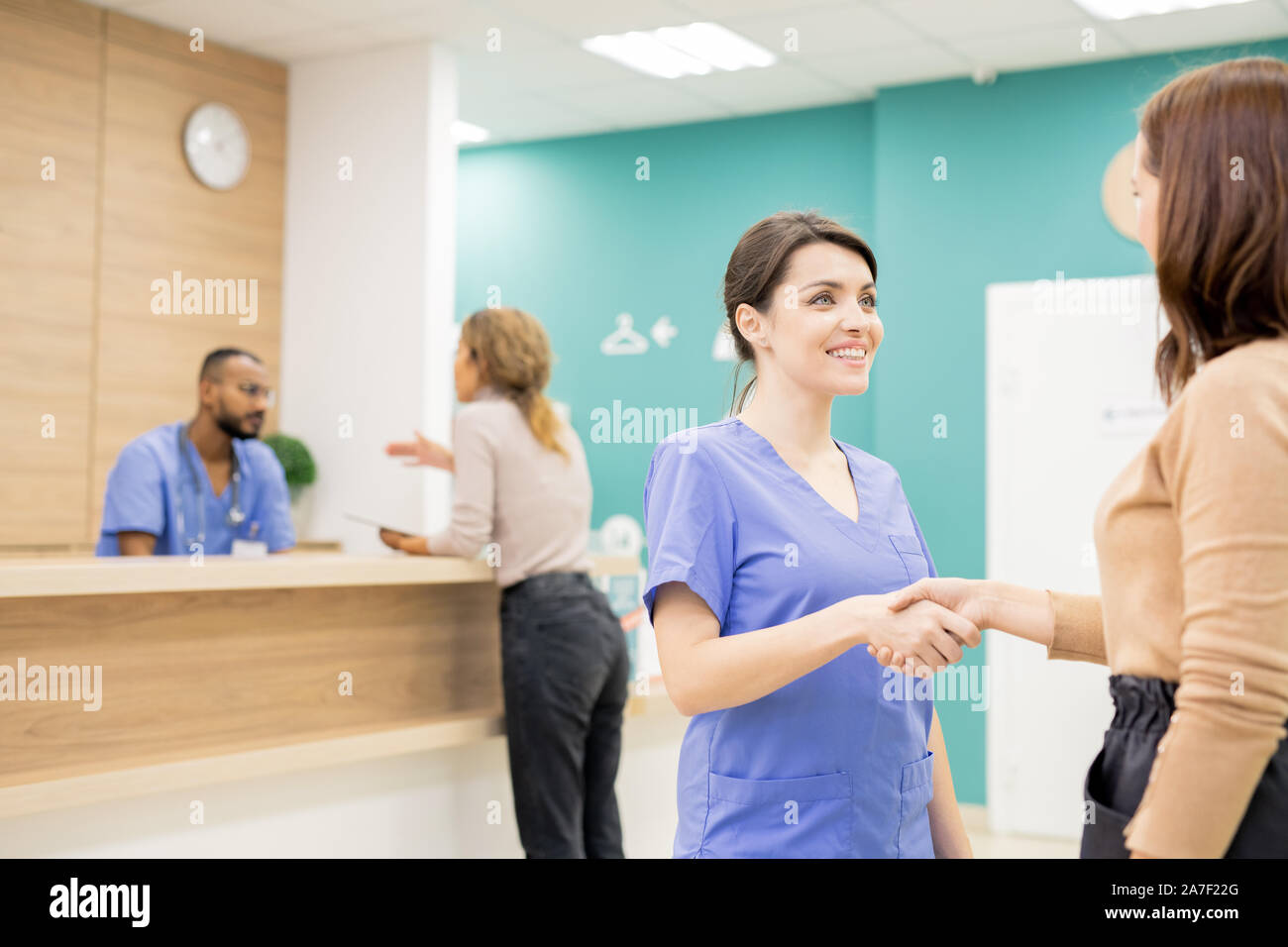 Pretty young smiling clinician in uniform shaking hand of female ...