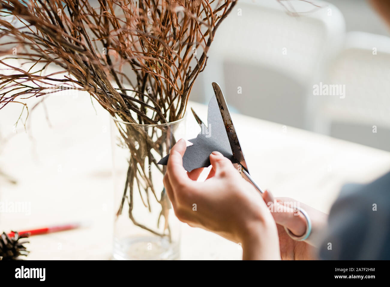 Hands of woman cutting paper bat with scissors to decorate dry branches ...