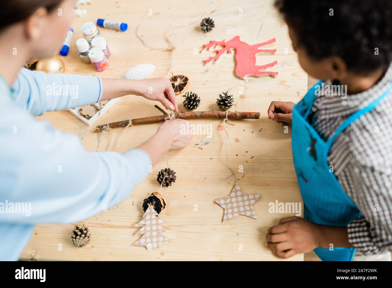 Hands of young teacher tying thread with handmade paper decorations to ...