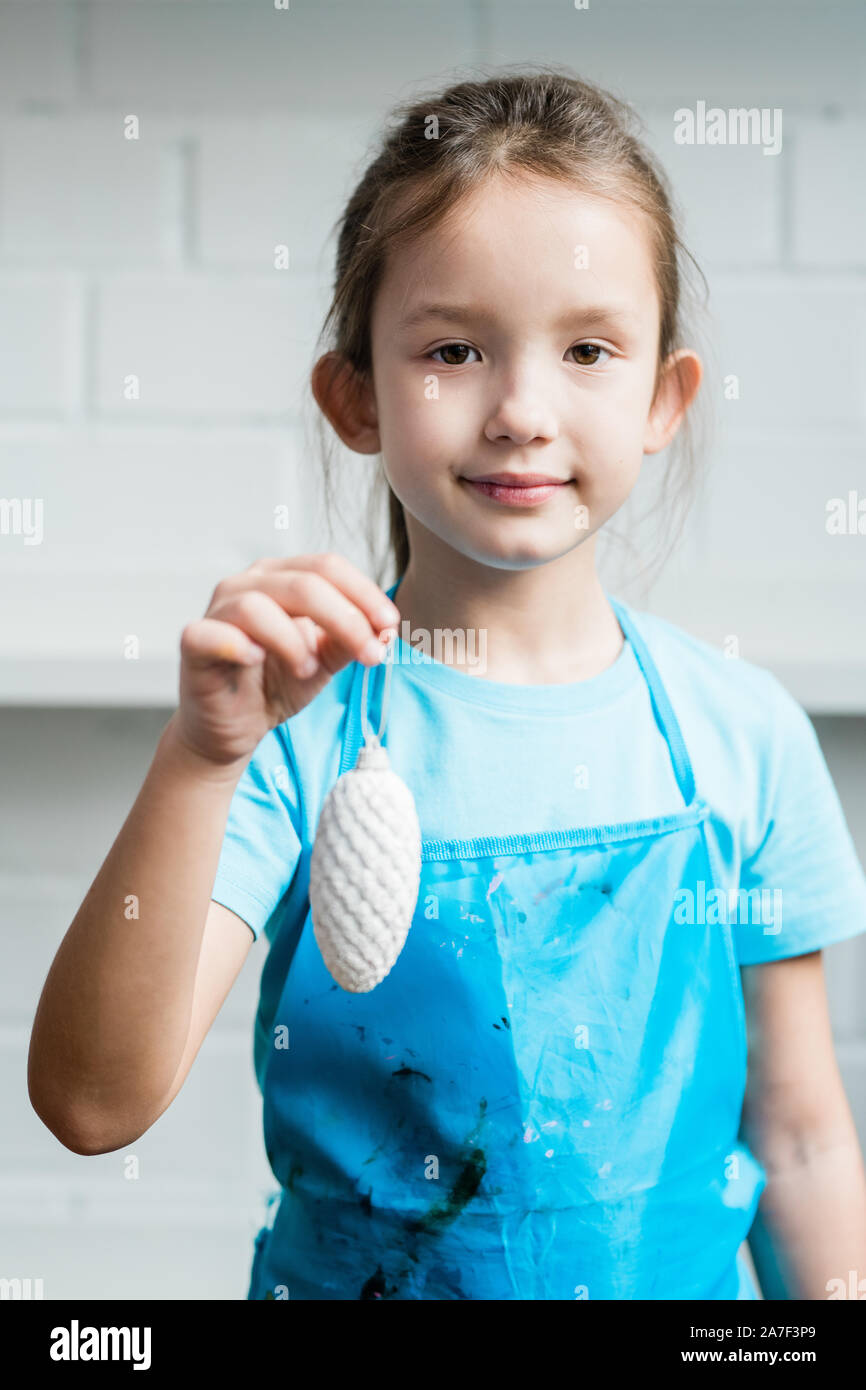 Cute girl in blue apron holding white painted handmade decorative ...