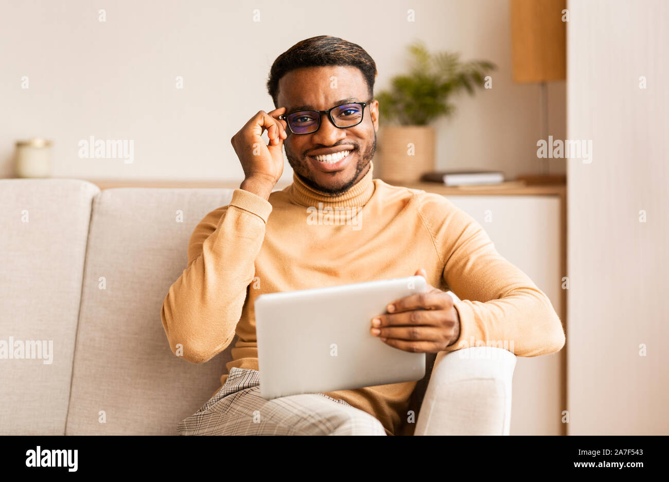 Millennial Black Guy Holding Tablet Smiling Sitting On Sofa Indoor ...