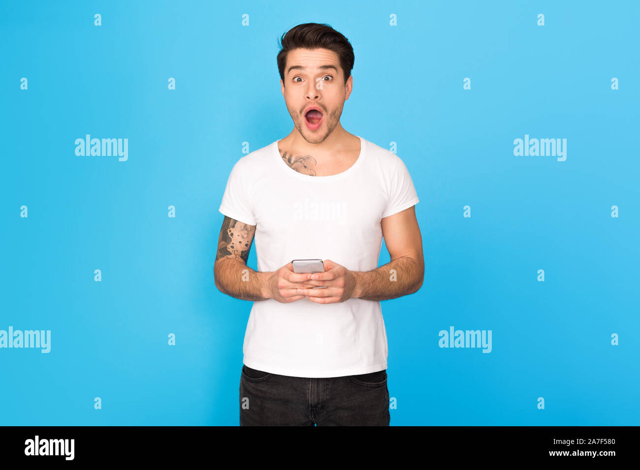 Shock content. Surprised guy holding smartphone, blue background Stock ...