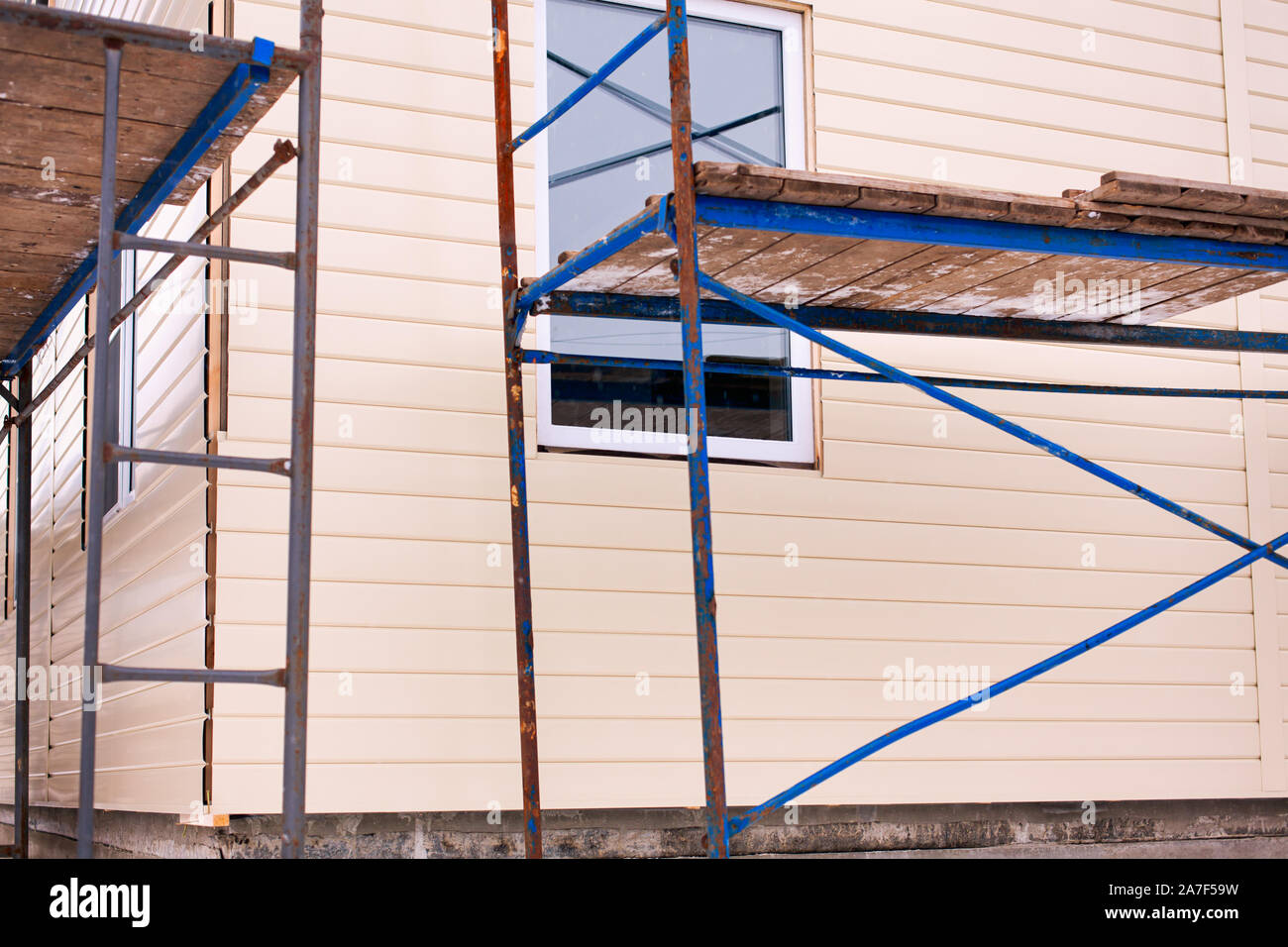 Beige siding covering the wall and scaffolding around the house. Close ...