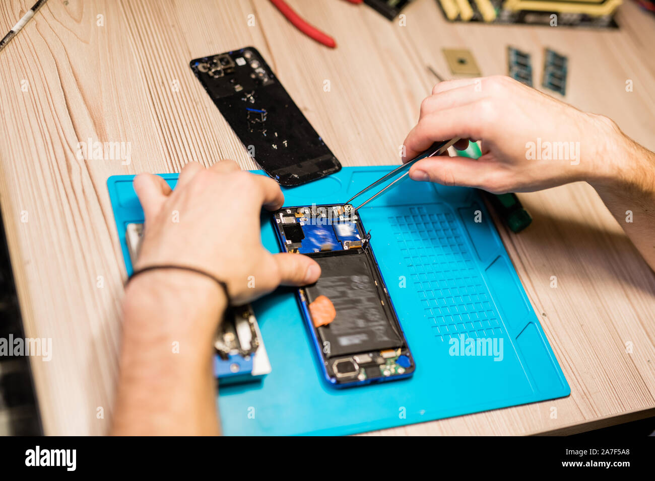 Hands of repairman over broken gadget using tweezers to fix tiny parts ...