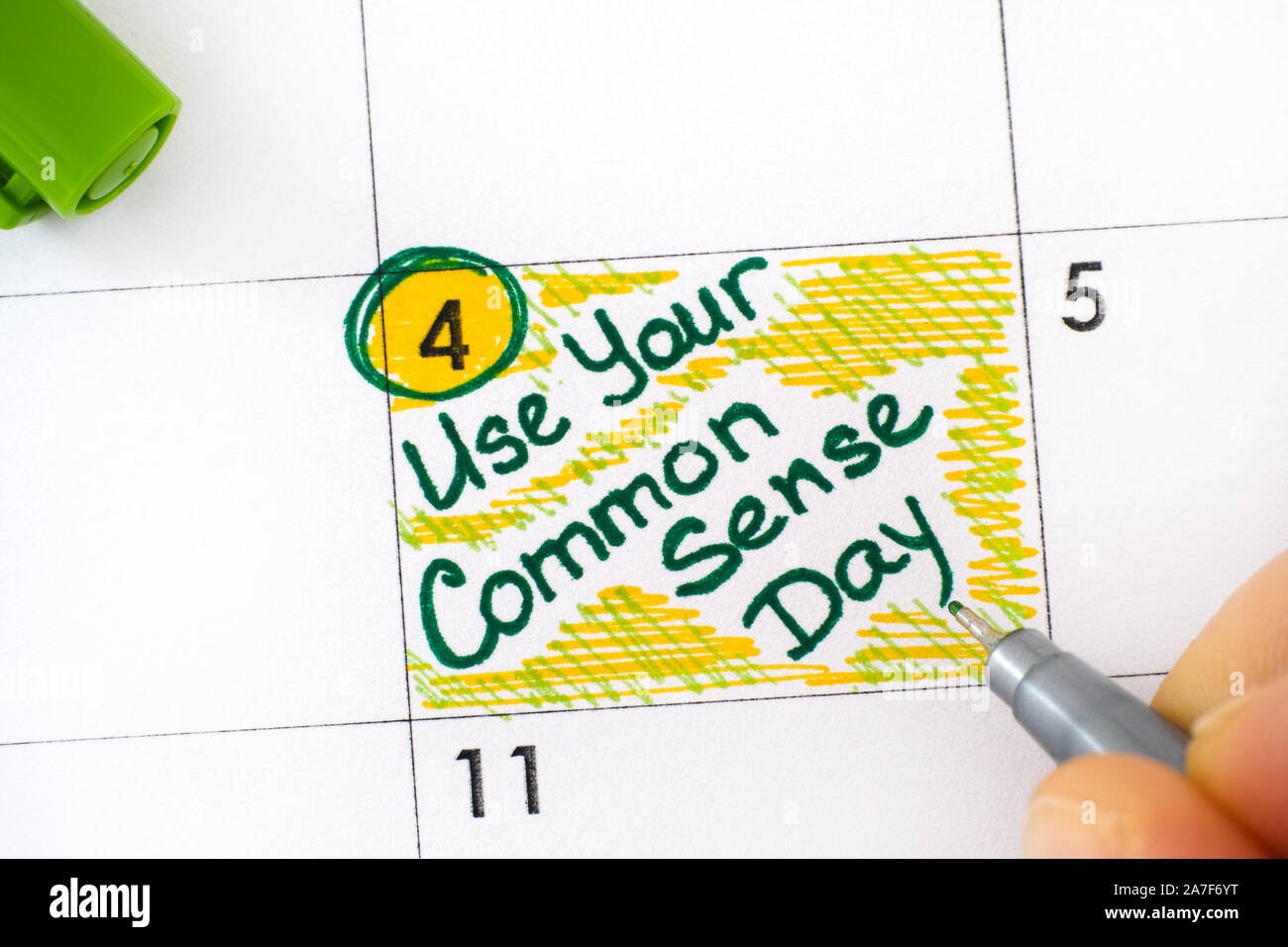Woman fingers with green pen writing reminder Use Your Common Sense Day ...