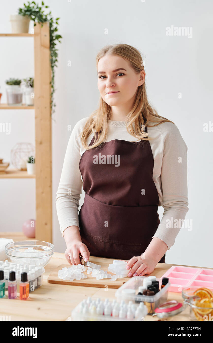 Happy young craftswoman standing by table in studio during soap making ...