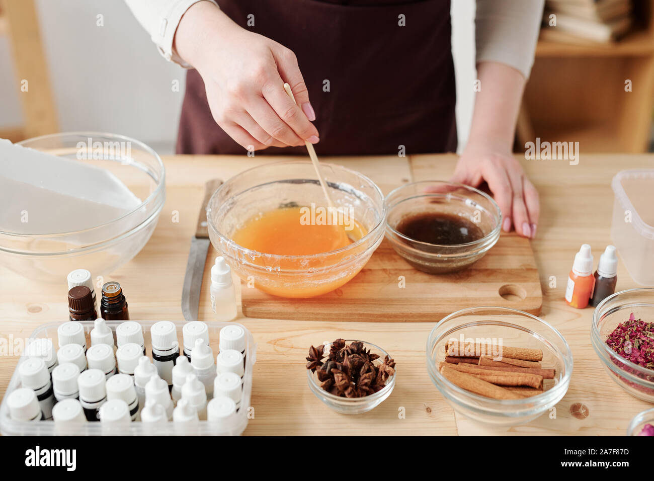 Craftswoman mixing liquid soap mass with orange essential oil in bowl ...