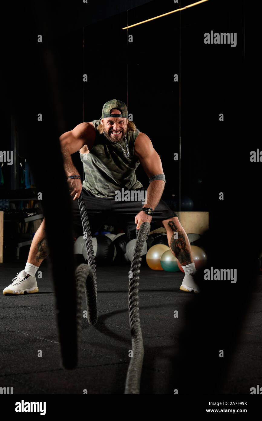 Inflated man tensely performs an exercise with ropes Stock Photo - Alamy