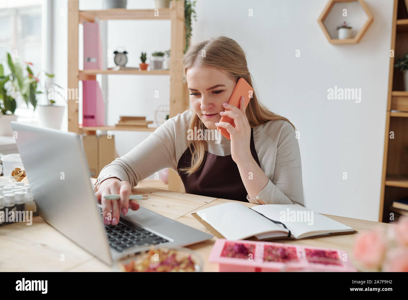 Busy female with smartphone sitting in front of laptop and calling her ...