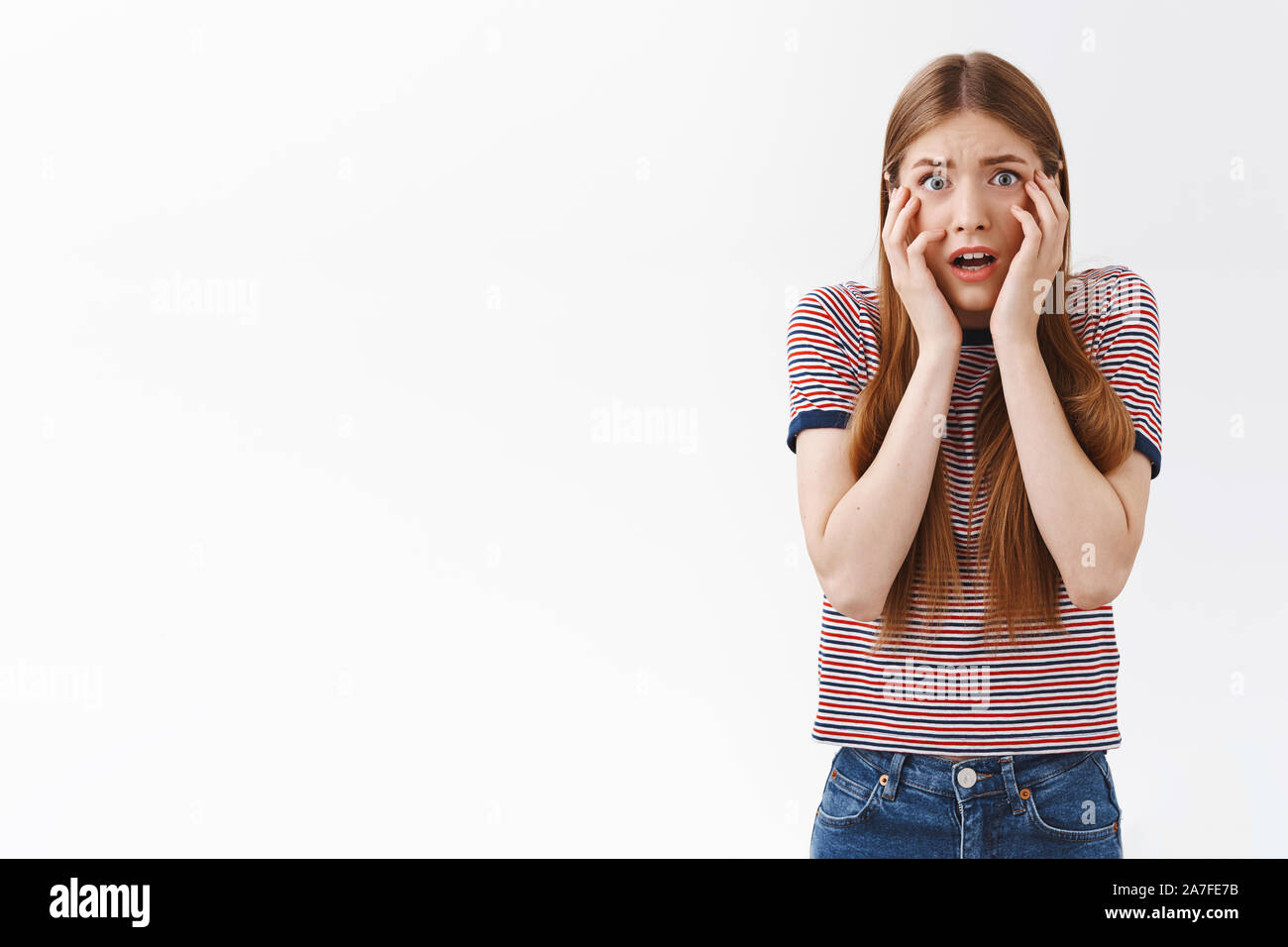 Scared timid cute woman in striped t-shirt hold hands on face, gasping ...