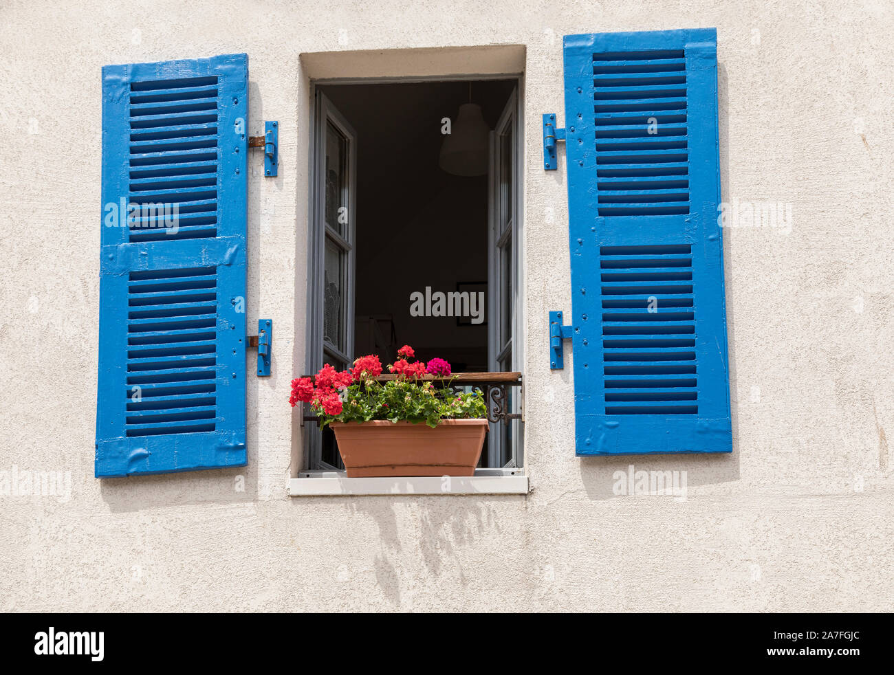 Traditional French bedroom window with blue shutters and geraniums in a ...