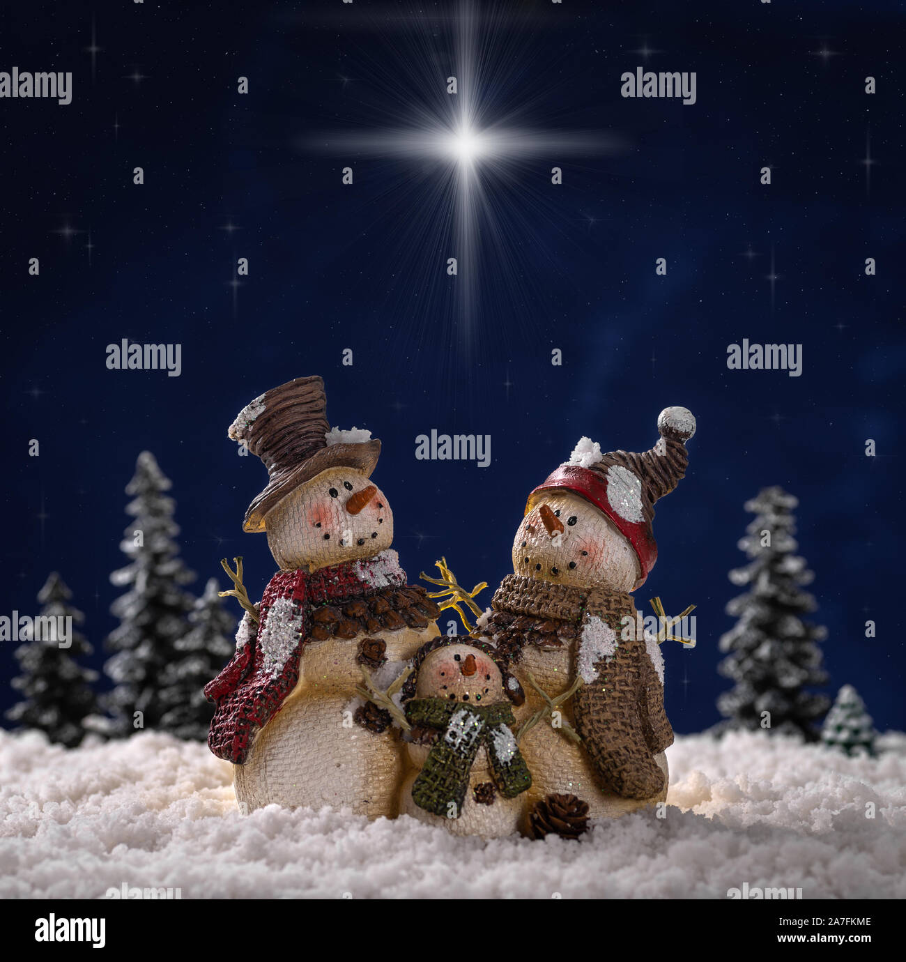 Holiday snowmen figurines on snowy surface against a night sky ...