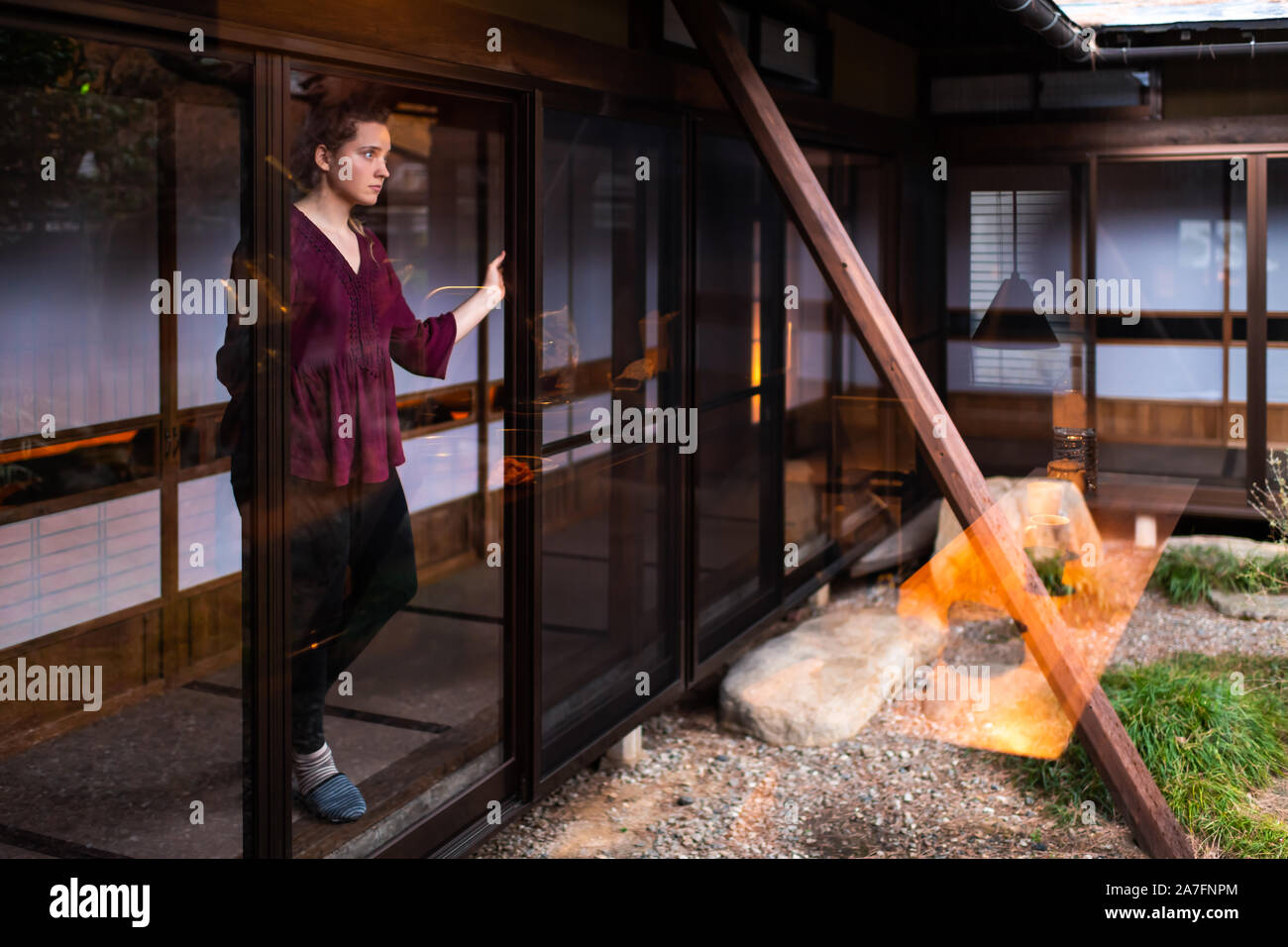 Young woman standing looking through window sliding door on small ...