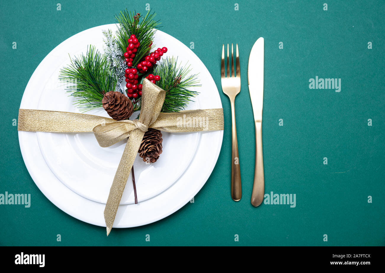 Christmas table setting. Gold cutlery and white set of dishes against ...