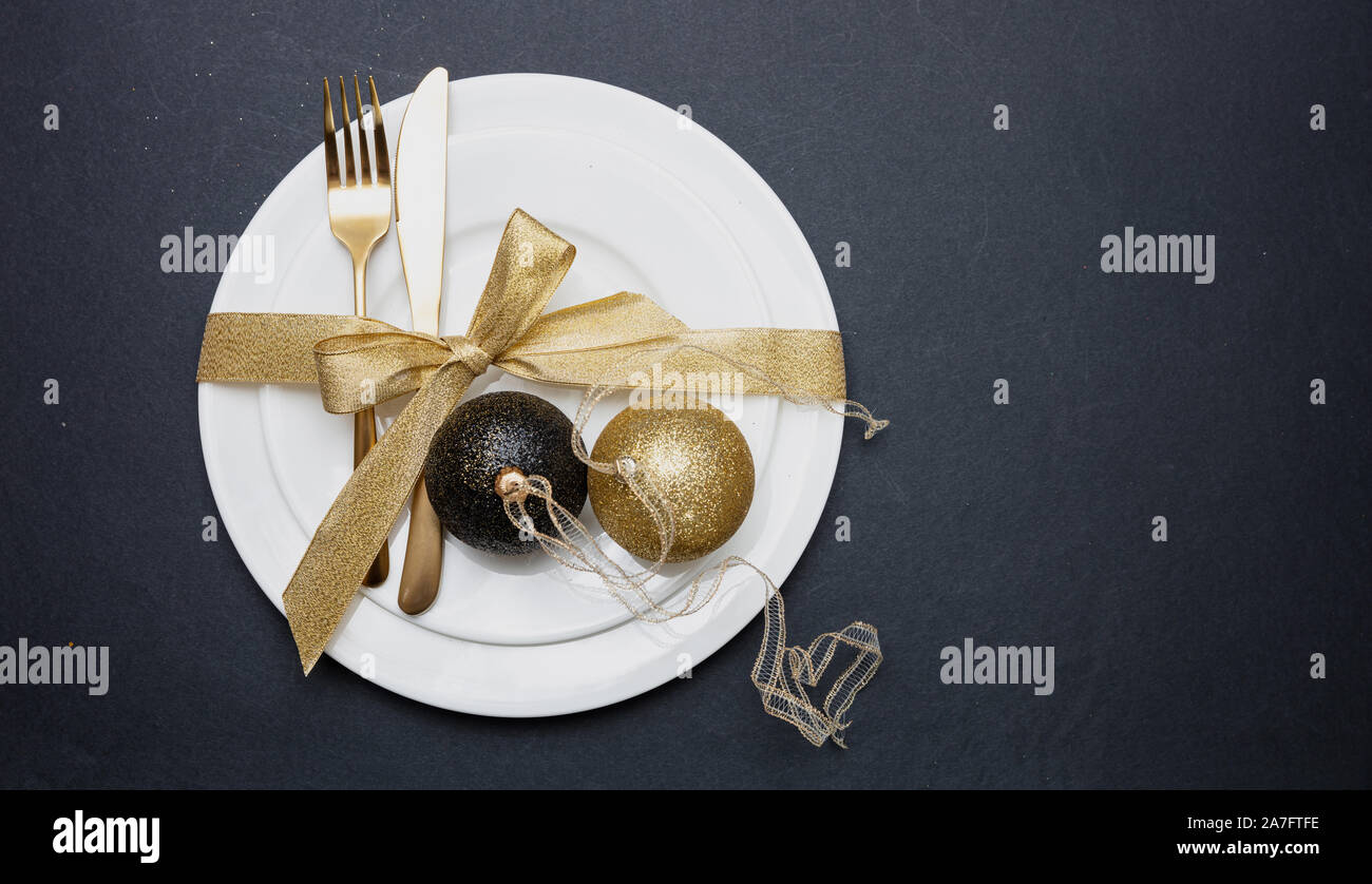 Christmas table setting. Gold cutlery and white set of dishes against ...