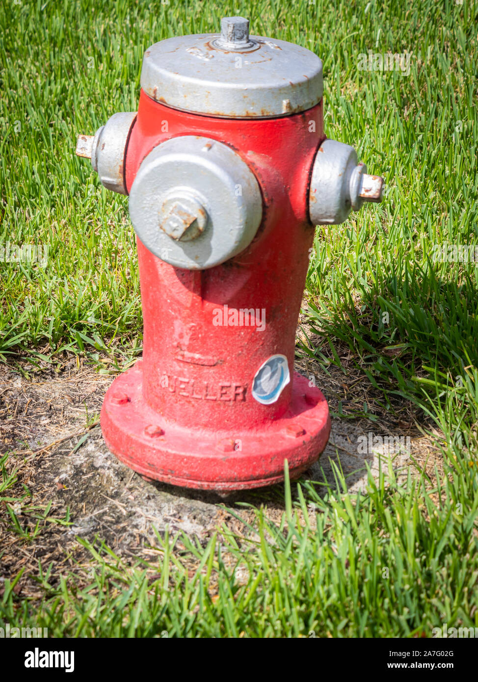 A bright red fire hydrant is installed on a grassy patch, ready for ...