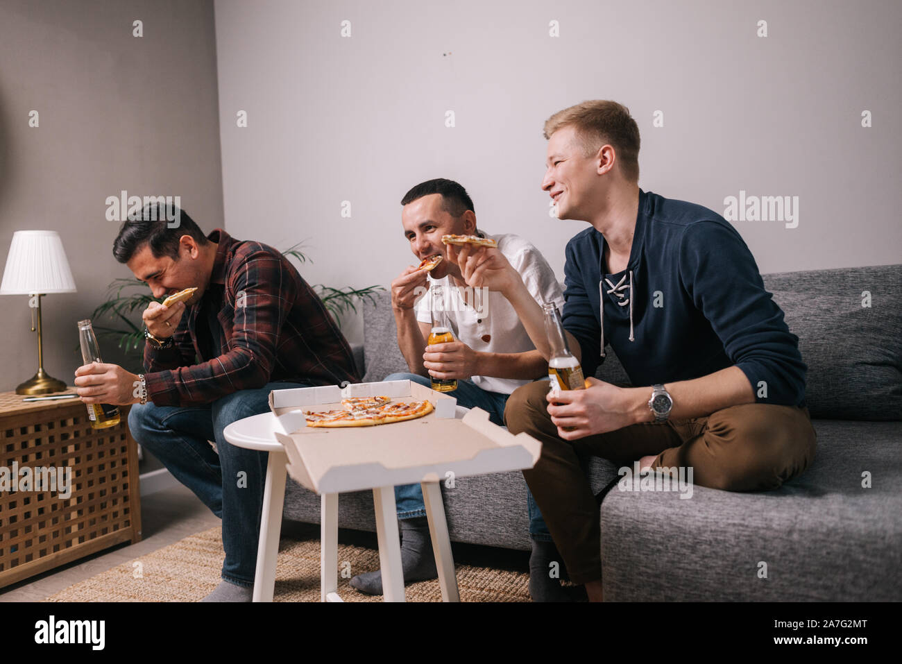 Group of young friends eating pizza, talking and carefree laughing ...