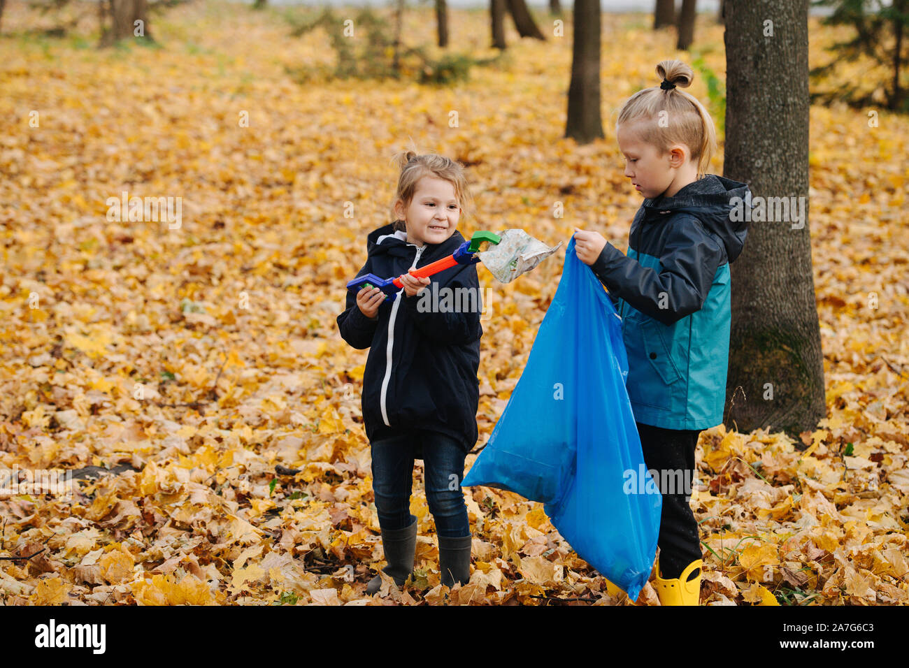 Little kid siblings collect trash using litter picker in a forest at ...