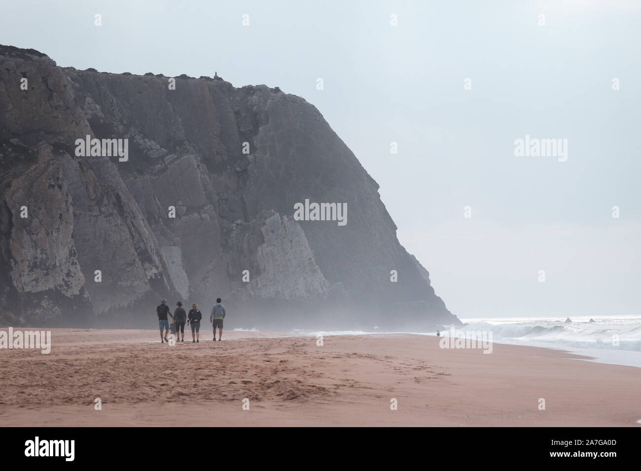Beach with a big cliff in background in a winter day with four people ...