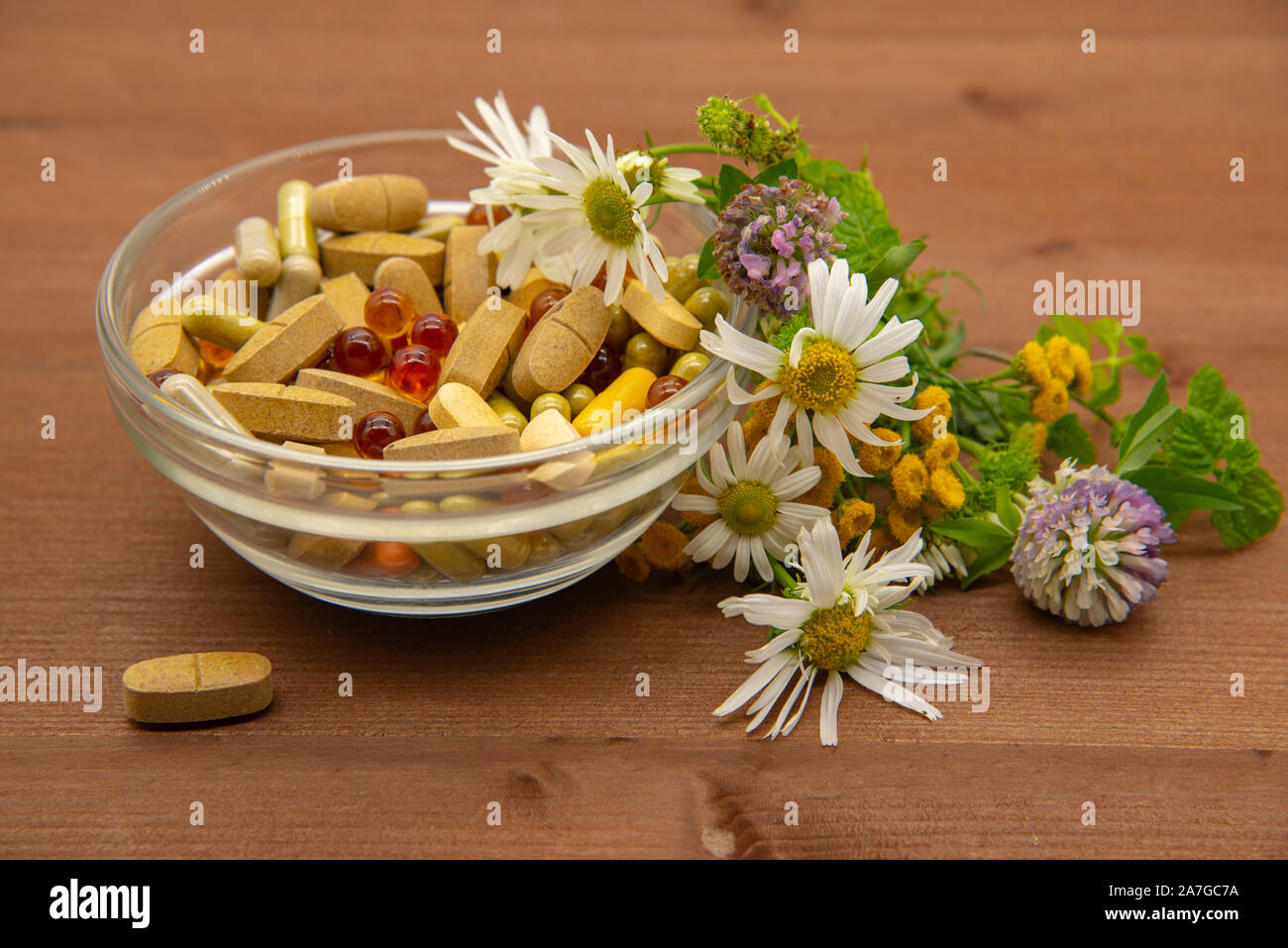 A bowl with various capsules and tablets, medicinal and aromatic herbs ...