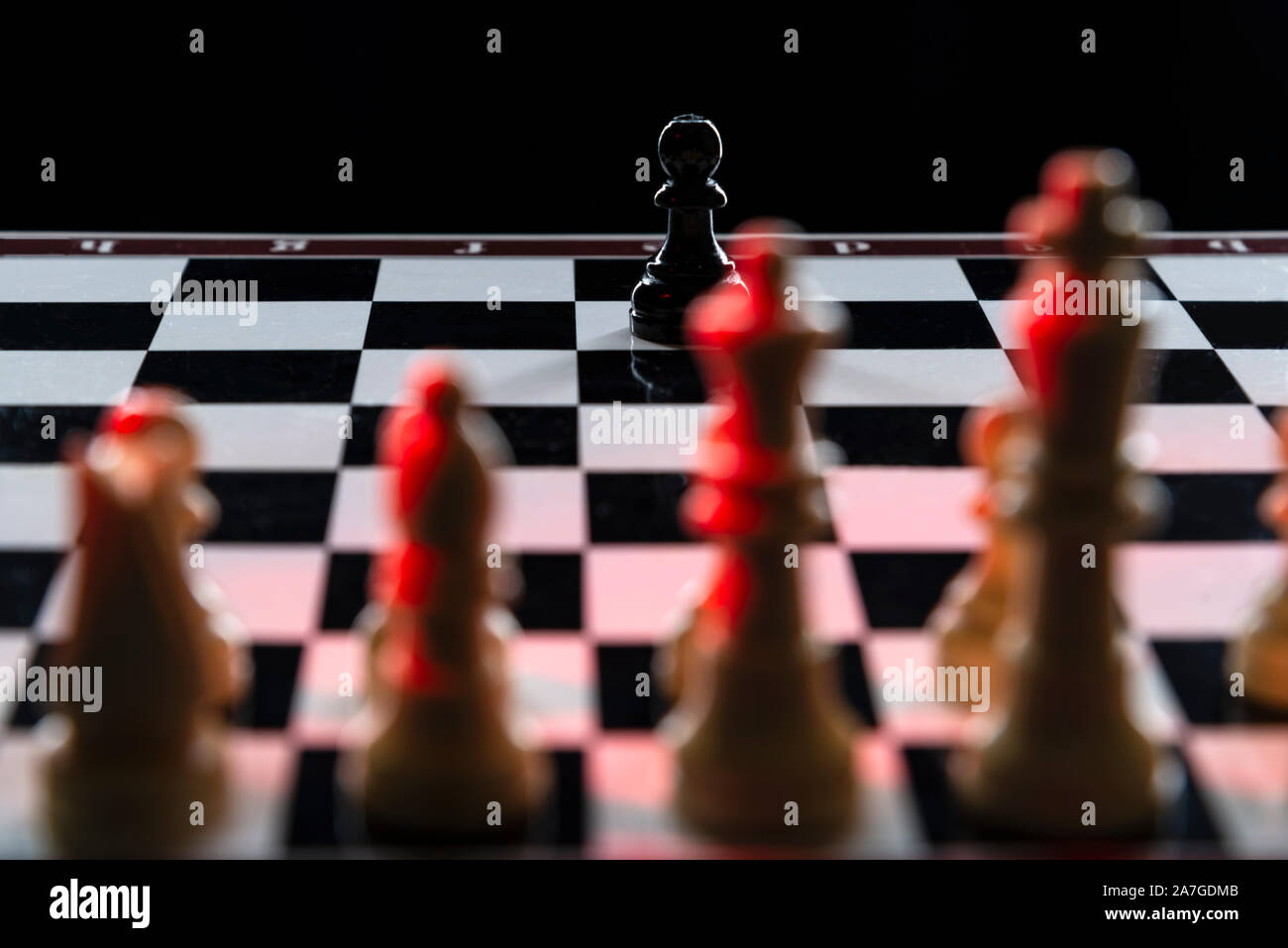 Black chess pawn against an army of white chess pieces on a chessboard ...