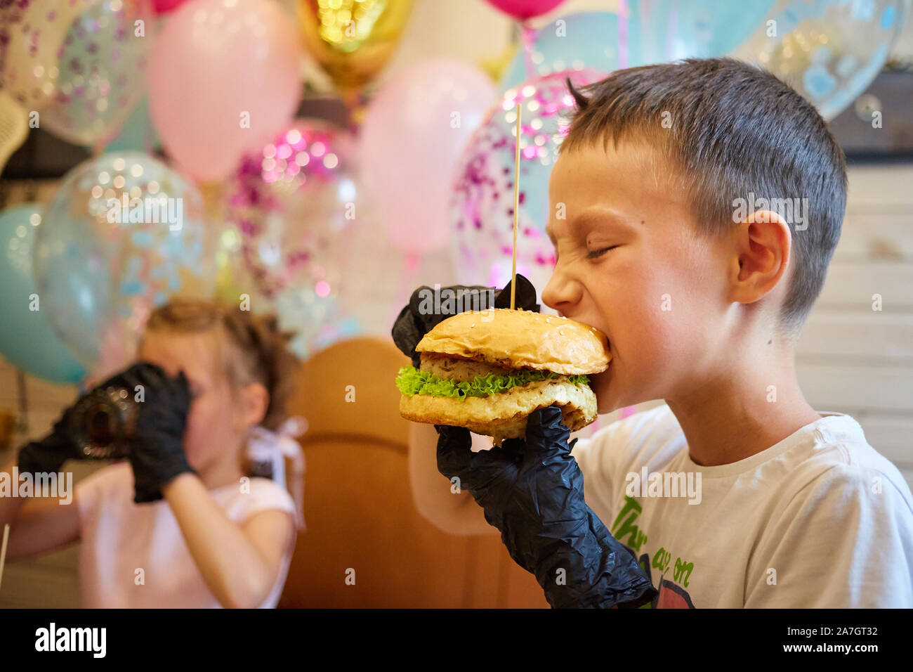 The handsome little boy eating burger in black rubber gloves Stock ...