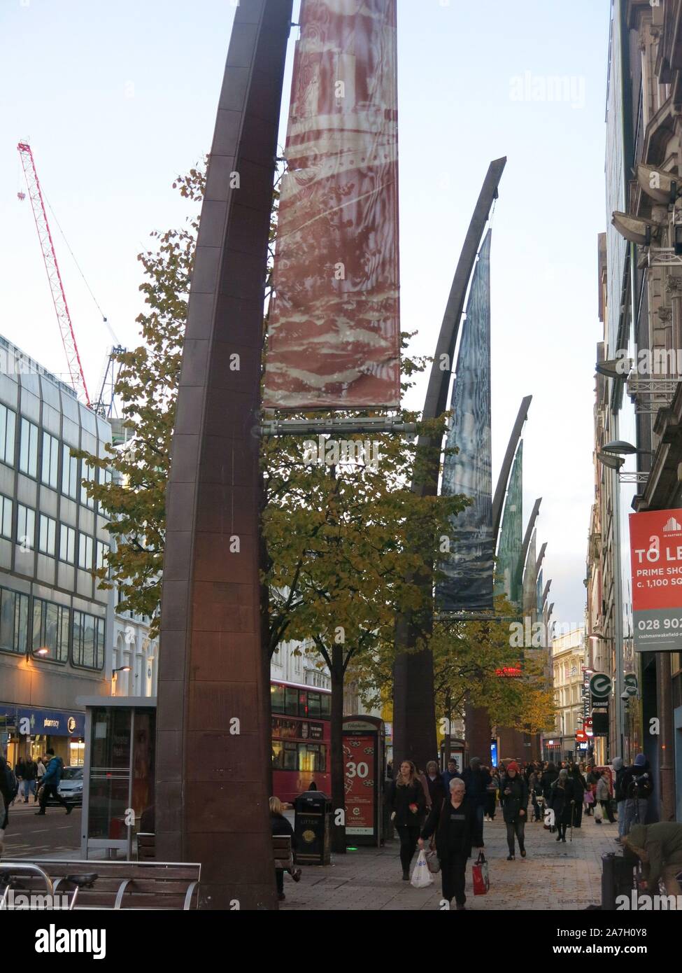 Photo of shopfronts, buses, tall trees, pedestrians and Titanic banners ...