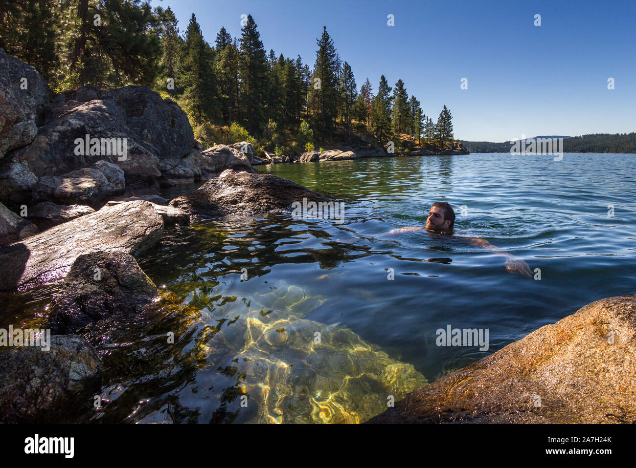 Man swimming in Coeur d' Alene Lake in northern Idaho with the rocks of ...