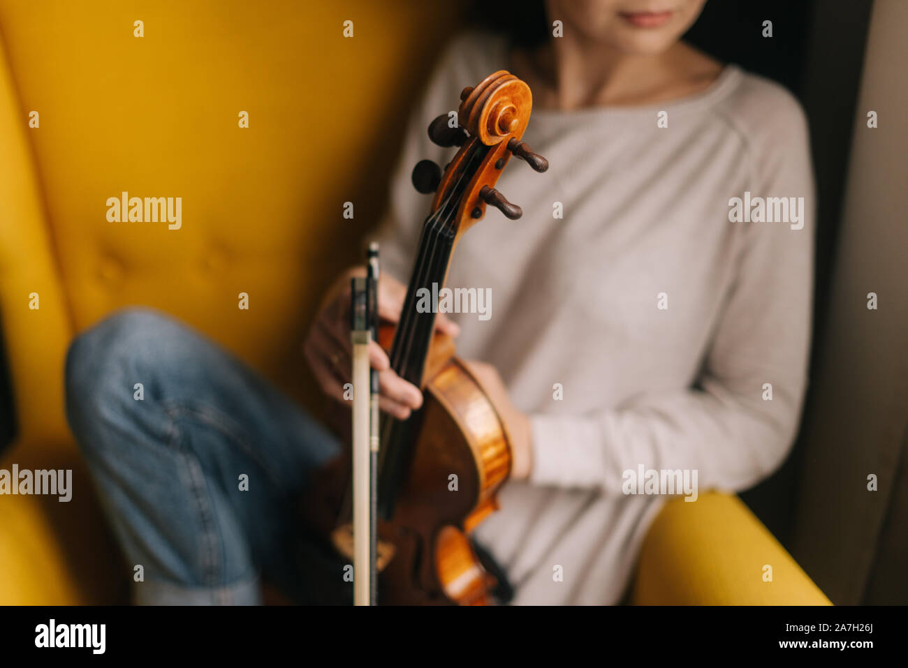 Beautiful young woman musician posing with a violin in a soft chair ...