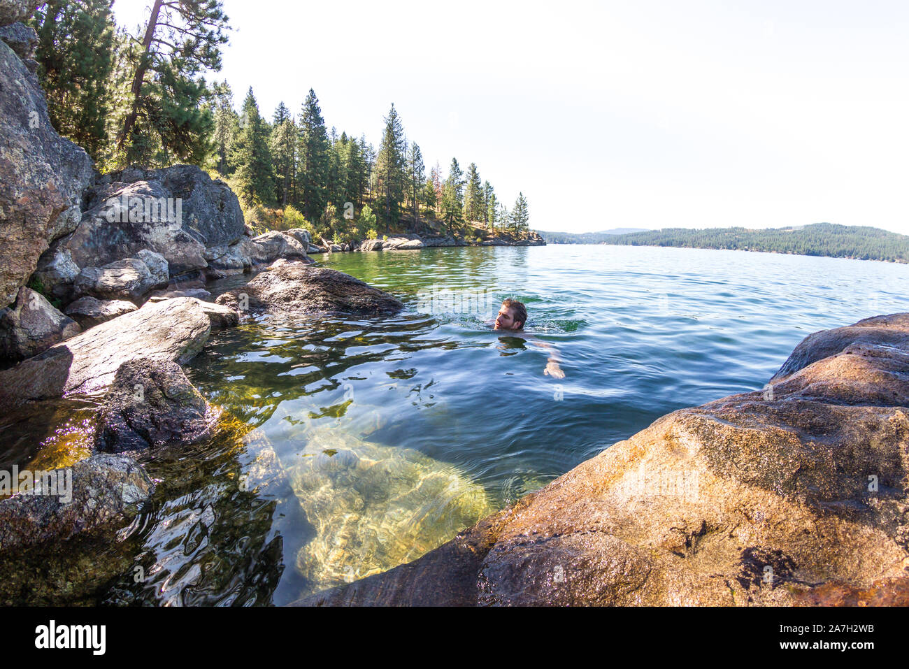 Man swimming in Coeur d' Alene Lake in northern Idaho with the rocks of ...