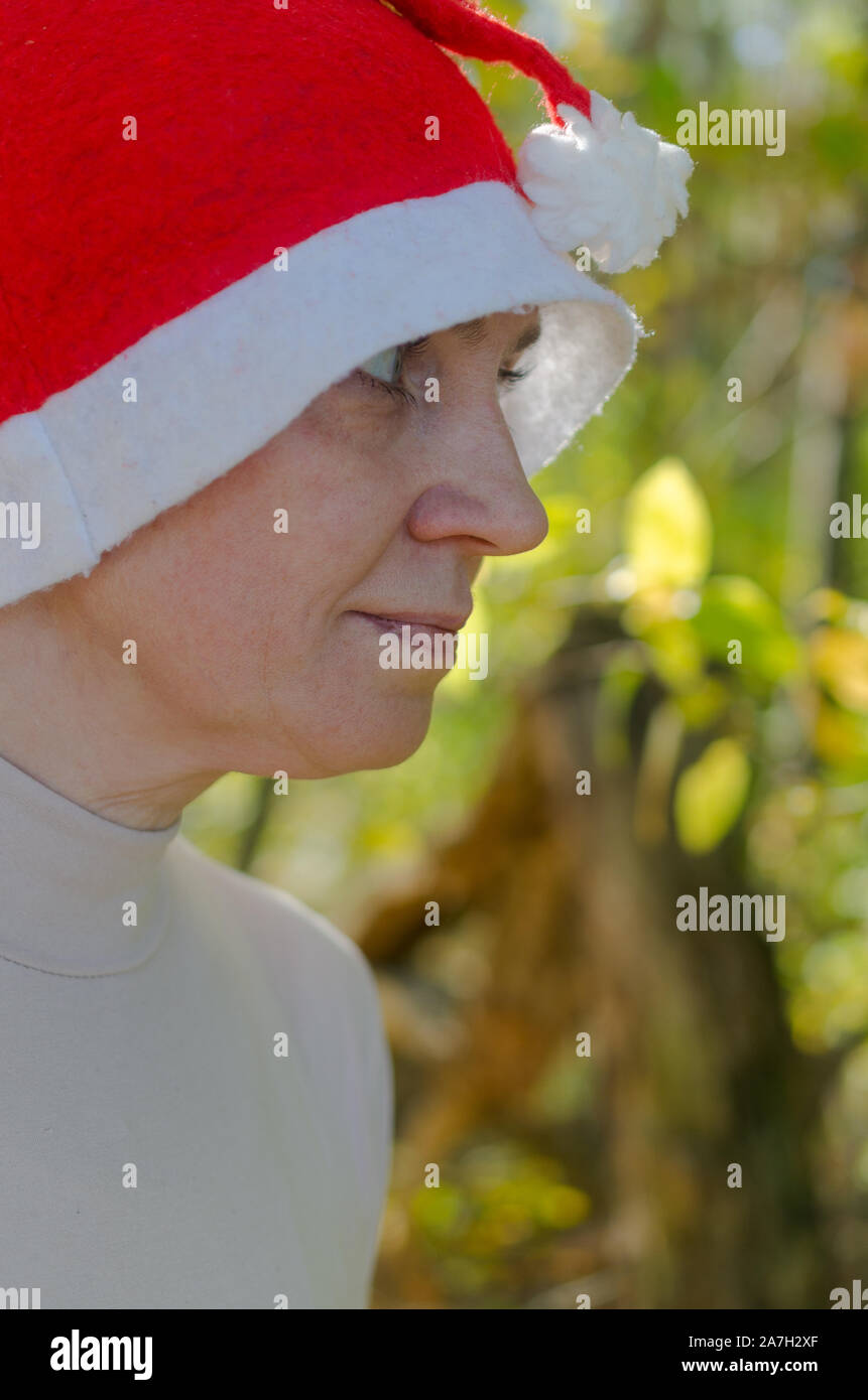 A woman in a hat of Santaclaus with a sly evil face among the autumn ...