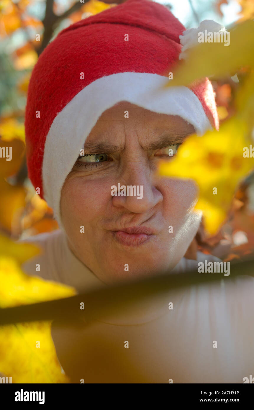 A woman in a hat of Santaclaus with a sly evil face among the autumn ...