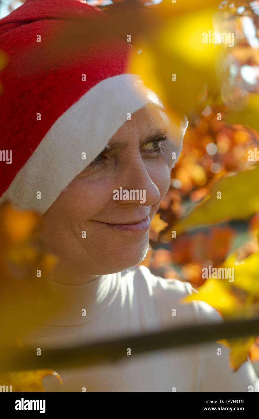 A woman in a hat of Santaclaus with a sly evil face among the autumn ...