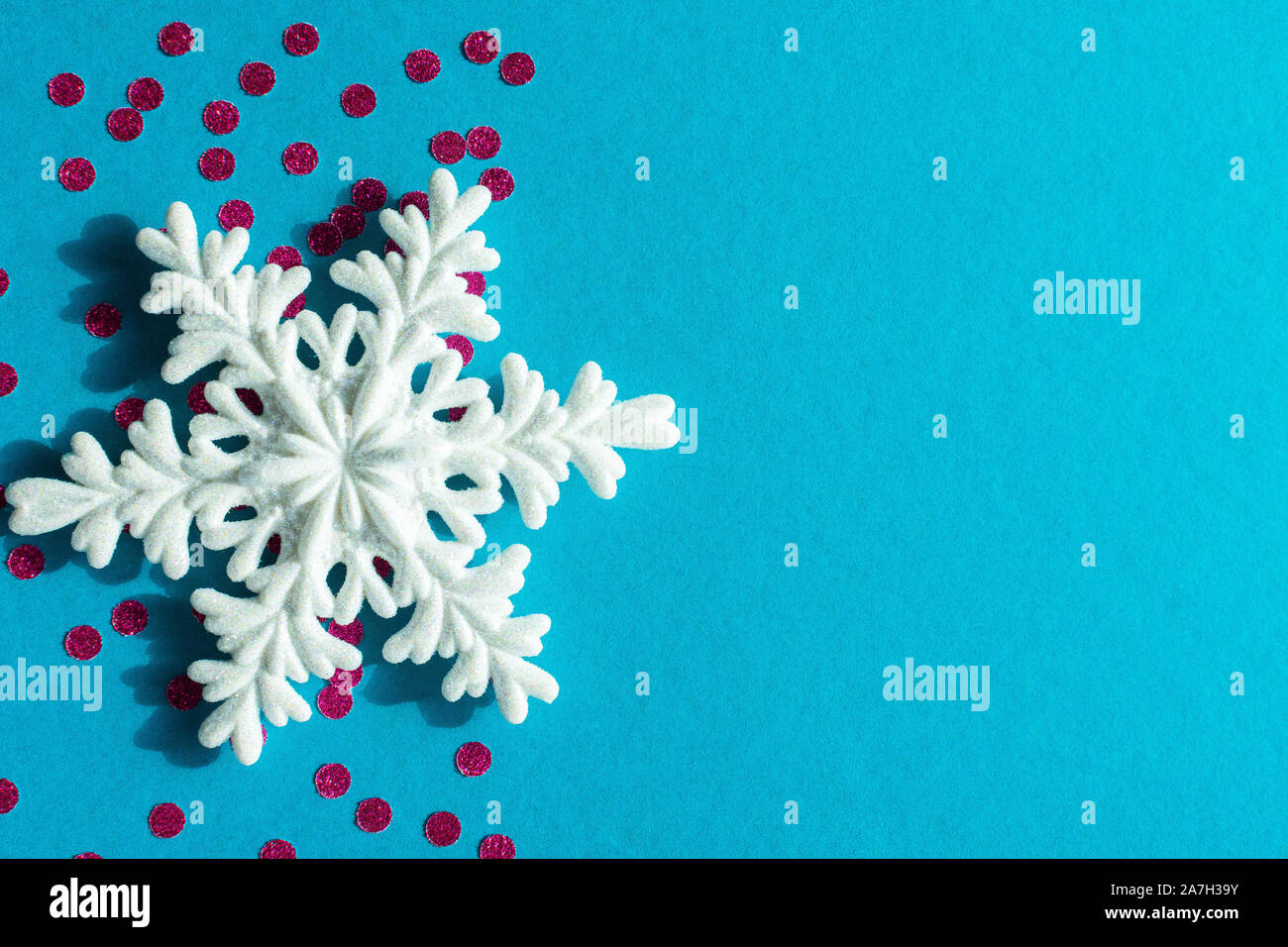White snowflake and bright pink round confetti on a blue background ...